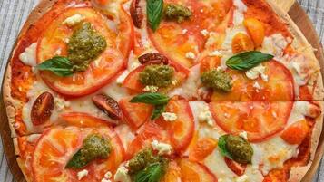 Pizza com rodelas de tomate, queijo e manjericão sobre uma tábua de madeira.
