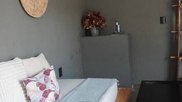 Quarto com uma cama, um cesto trançado fixado na parede, uma pequena mesa com um vaso e uma estrutura de teto geométrica.