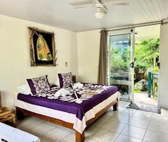 Quarto com cama, almofadas, ventoinha no teto e vista para o verde através de uma porta de vidro.