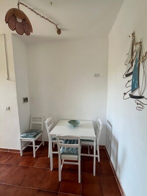Uma área de refeições com uma mesa branca, quatro cadeiras e um lustre.