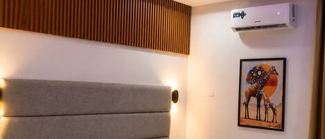 Quarto de hotel moderno com uma cama grande, cabeceira com iluminação embutida, ar condicionado e uma obra de arte pendurada na parede.
