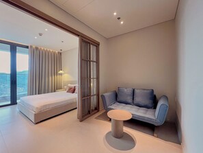Quarto de hotel moderno com cama, sofá, uma mesinha e uma janela ampla com vista.