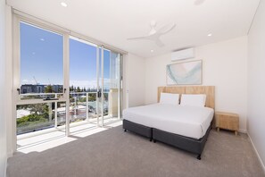 Quarto moderno com cama grande, ventilador de teto e vista da cidade através de janelas do chão ao teto.