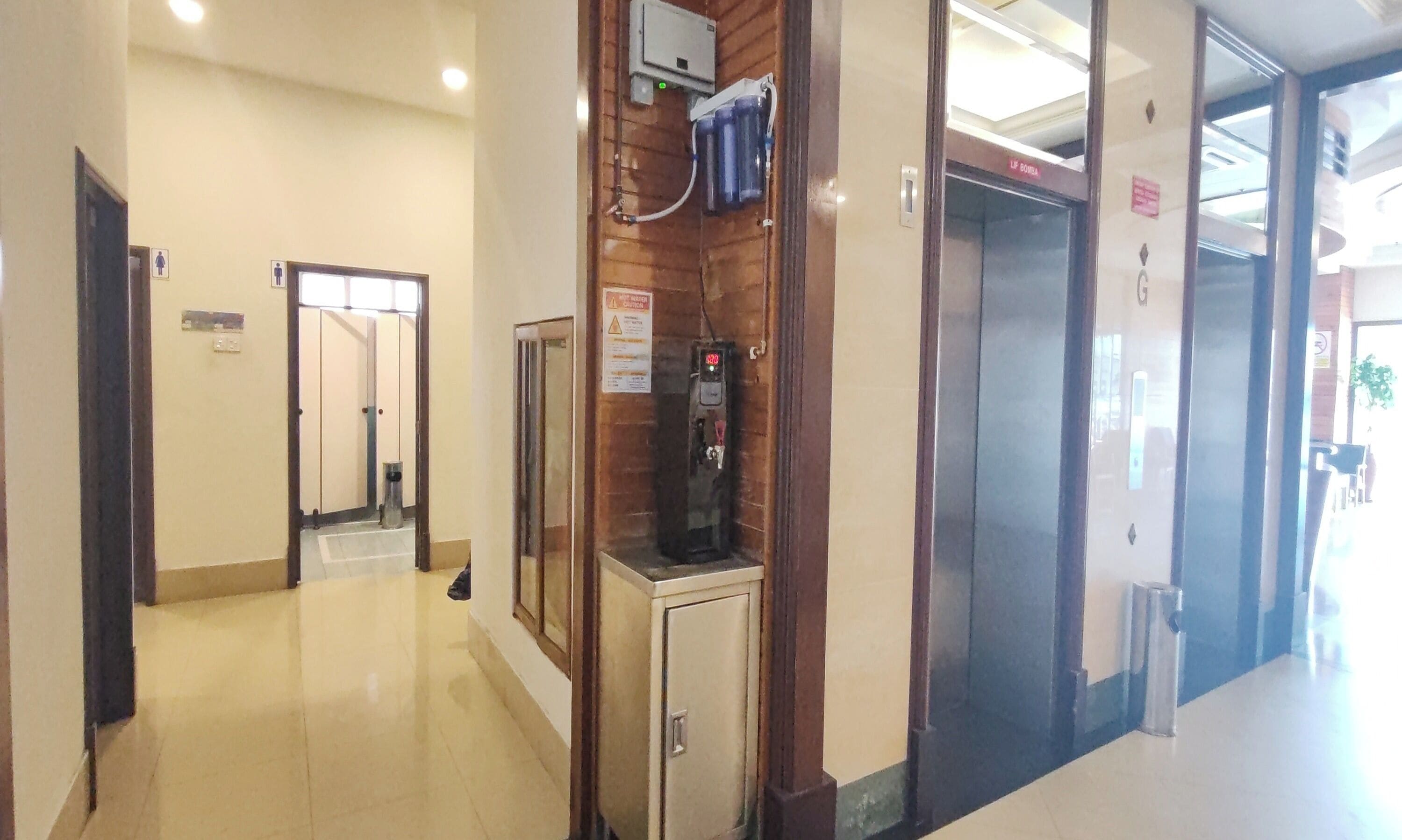 Um corredor com um bebedouro, um alarme de incêndio e uma porta identificada como 'LF BOWSA'.