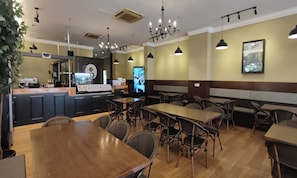 Interior de restaurante com mesas e cadeiras de madeira, um balcão com menu e uma tela de televisão.