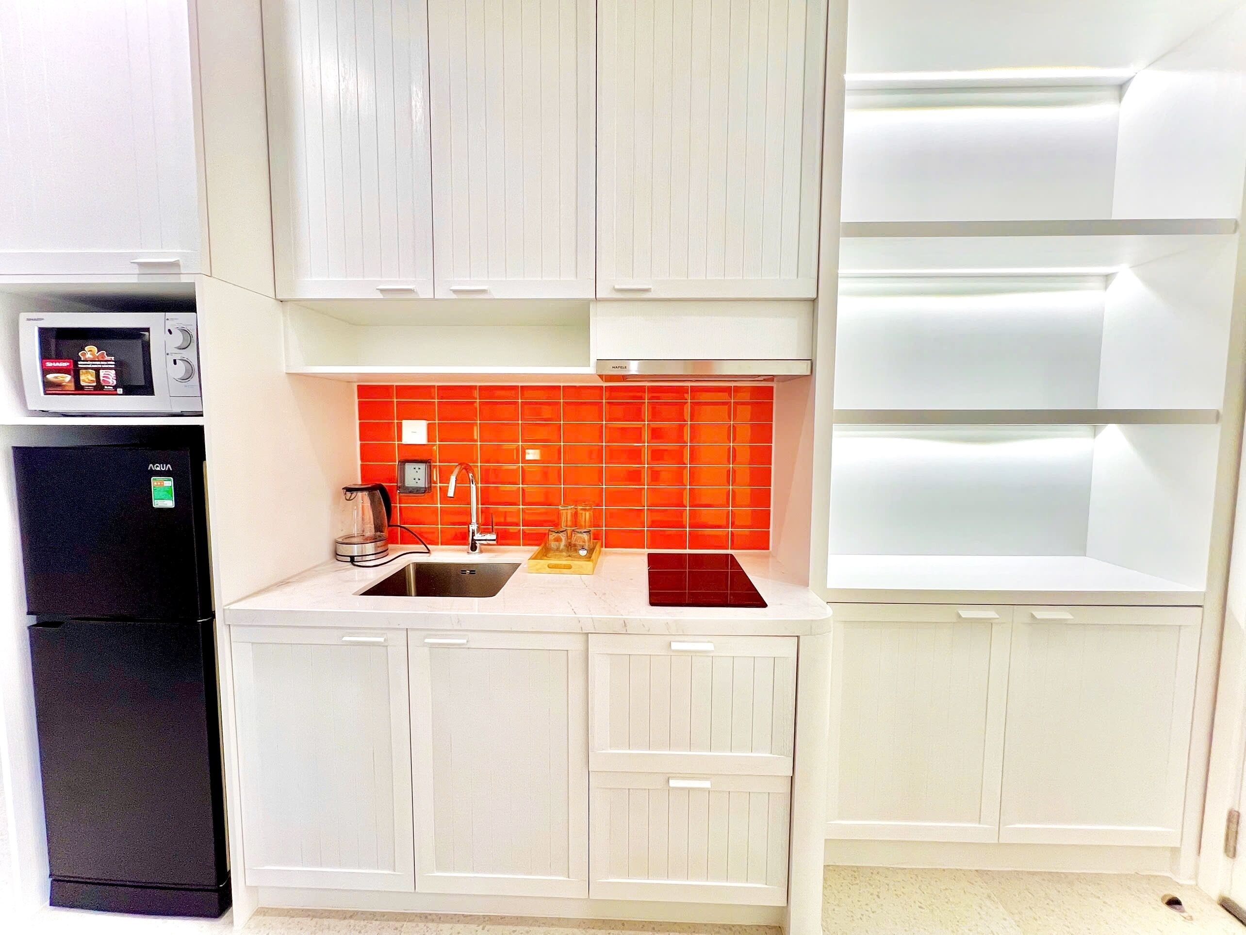 Uma cozinha com armários brancos, painel de azulejos vermelhos, geladeira preta e micro-ondas.