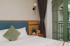 Uma cama bem arrumada com um travesseiro verde, uma mesinha de cabeceira com um livro e uma pequena planta, e uma luminária na parede.