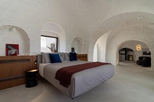 Quarto espaçoso com uma cama grande, cabeceira de madeira e vista através de uma janela em arco.