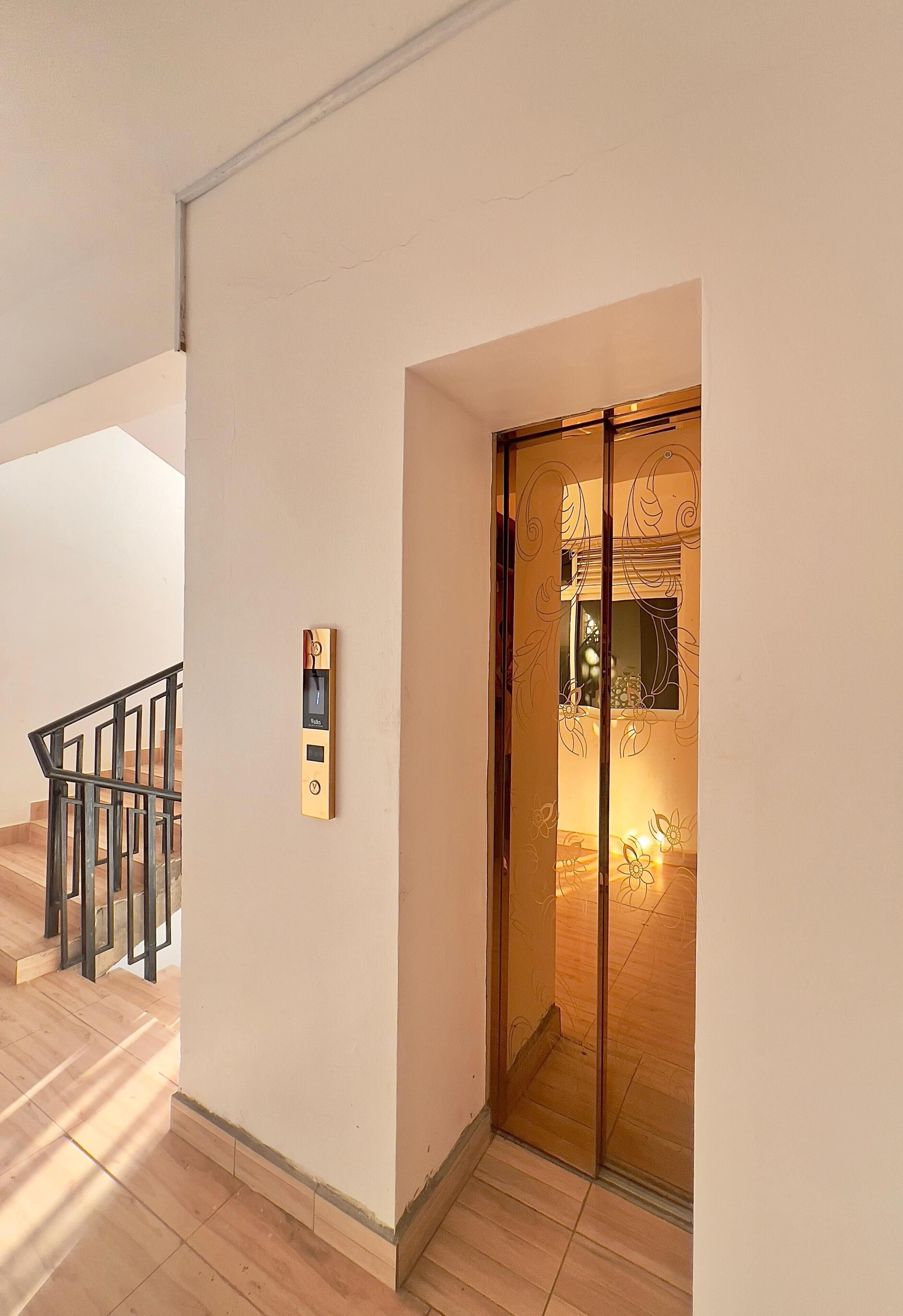 Um interior moderno com escada de madeira, elevador embutido na parede e painel decorativo com motivos florais.