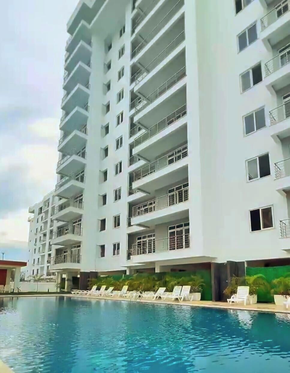Um edifício residencial com vários andares, varandas e uma piscina com espreguiçadeiras.