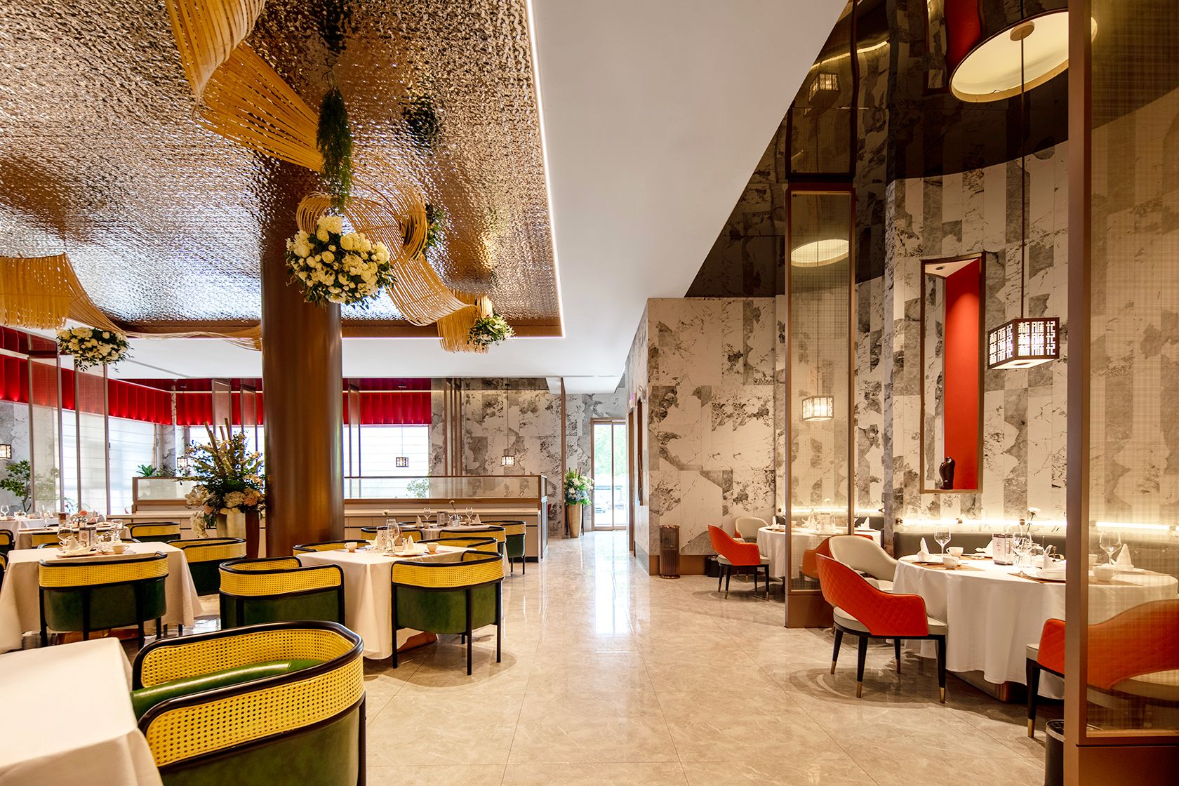 Ampla área de refeições de hotel, com várias mesas e cadeiras, teto alto com detalhes decorativos e design de interiores moderno.