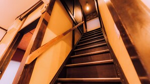 Uma escada de madeira com corrimão, um luminário acima e uma porta no topo.