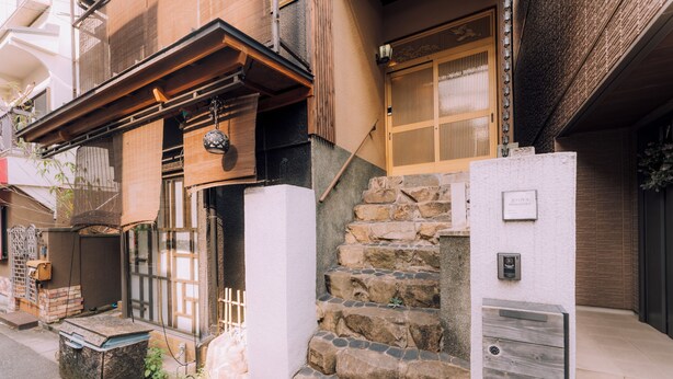 Um edifício tradicional japonês com escadaria de madeira, porta deslizante e pequena varanda.