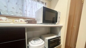 Uma cozinha com micro-ondas, torradeira e cozedor de arroz numa prateleira.