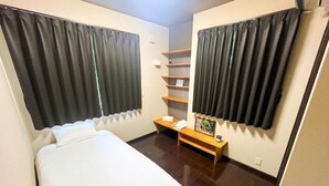Quarto de hotel com cama, mesa de cabeceira, prateleira com objetos e cortinas.