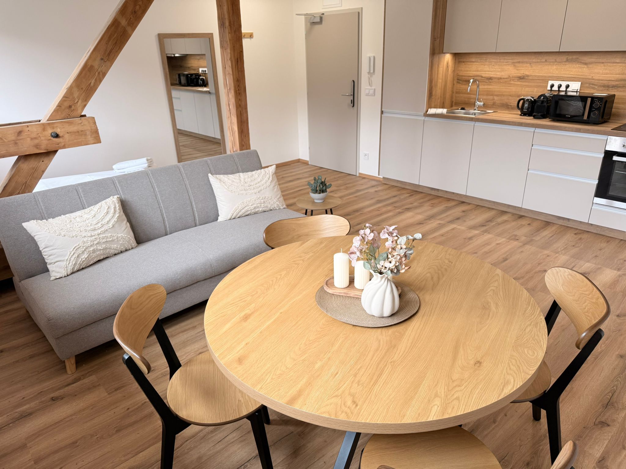 Sala moderna com mesa redonda de madeira, sofá cinza e cadeiras de madeira.