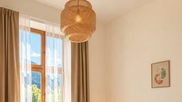 Quarto com cama de madeira, janela com cortinas, luminária fixada na parede e quadro emoldurado.
