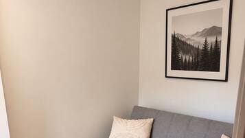 Um quarto com sofá cinza, tapete tecido e um quadro com uma paisagem de floresta na parede.