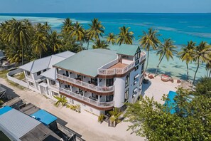 Hotel com vários andares, varanda, localizado na praia, com palmeiras e piscina.