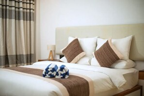 Cama bem arrumada com manta listrada, dois travesseiros e um objeto decorativo sobre ela.