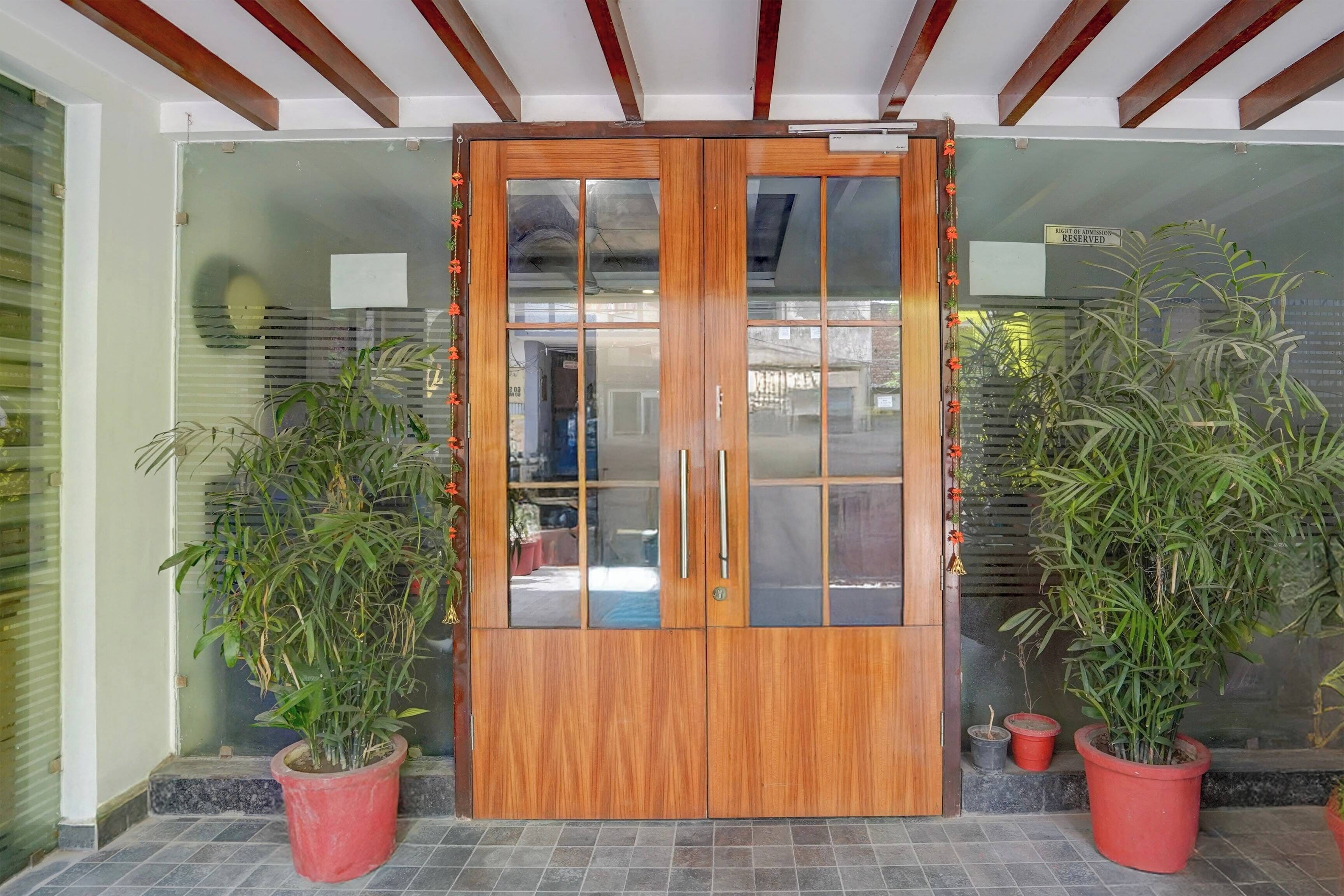 A wooden double door with glass panels, flanked by potted plants.