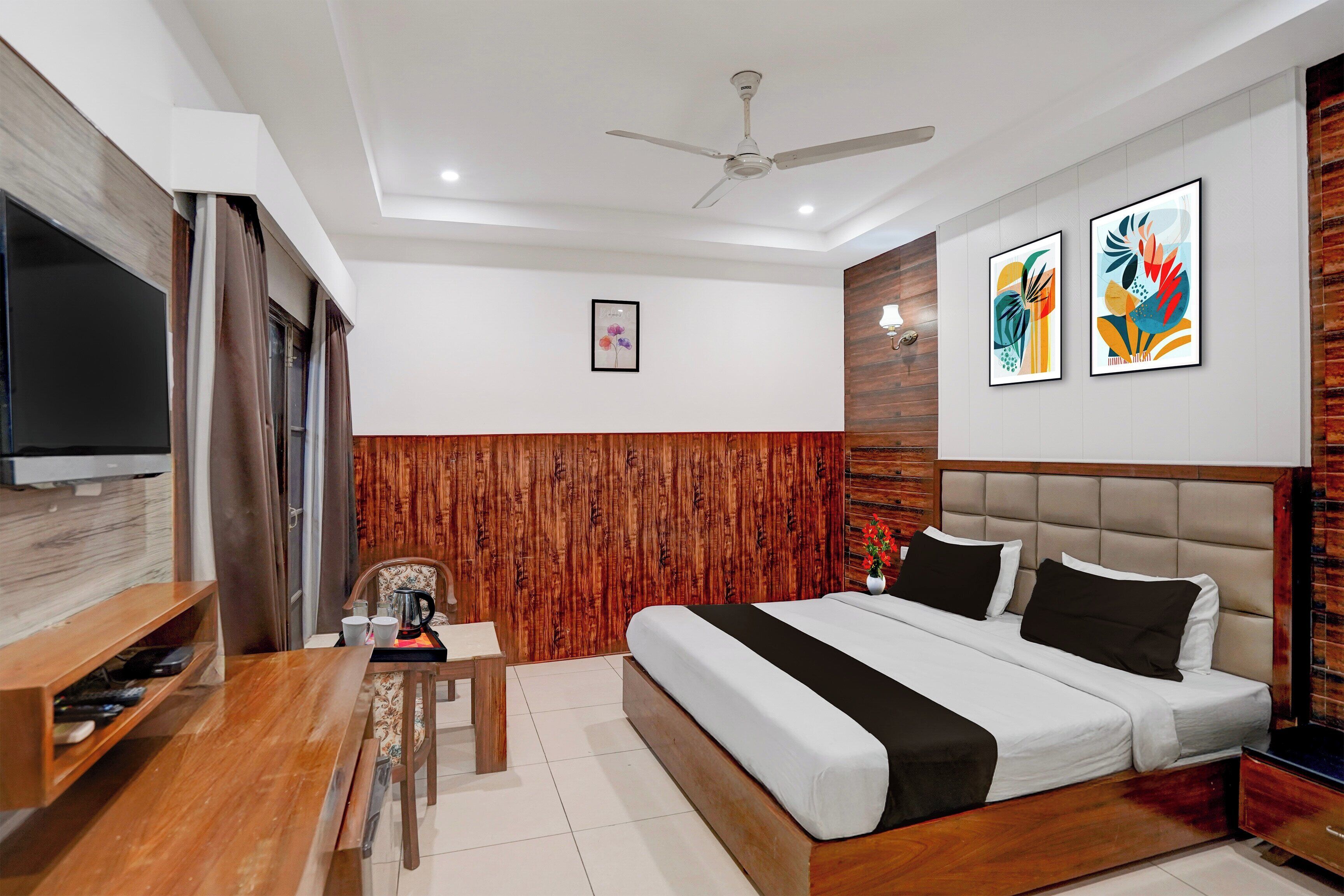 A modern hotel room with a bed, a desk, a television, and artwork on the walls.