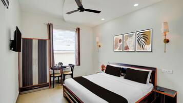 Quarto de hotel com cama, escrivaninha, cadeira, ventoinha no teto e obras de arte nas paredes.