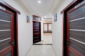 Um corredor com portas numeradas 104, 105 e 103, que dá acesso a um quarto com uma janela grande e cortinas.
