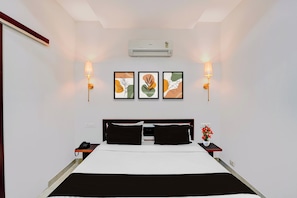 Quarto de hotel com cama, duas mesas de cabeceira, ar condicionado e obras de arte na parede.
