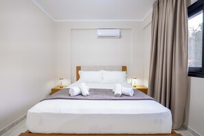 Quarto de hotel com uma cama, duas mesas de cabeceira, uma janela com cortinas e um ar condicionado.