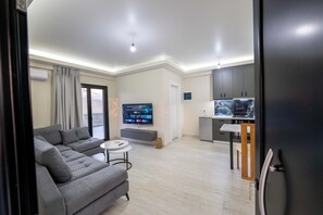 Uma sala de estar moderna com um sofá cinzento, uma mesinha redonda e uma televisão de tela plana fixada na parede.