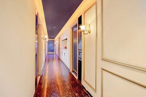 Um corredor de hotel com piso de mármore, arandelas e uma porta com número.