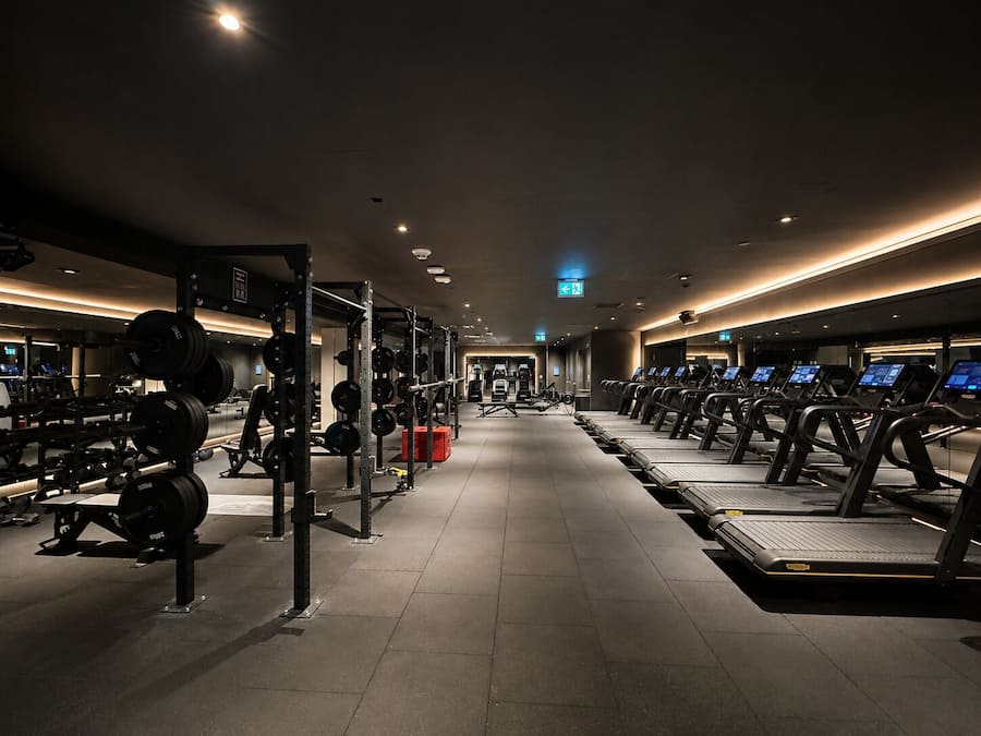 Uma academia com esteiras, equipamentos de musculação e um espelho grande na parede.