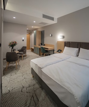 Quarto de hotel com cama grande, uma mesa de escritório, uma cadeira e uma pequena mesa com um vaso de flores.