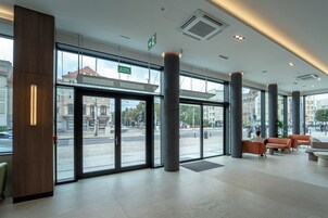Um hall de hotel moderno, com grandes portas de vidro, um balcão de recepção e áreas de estar.