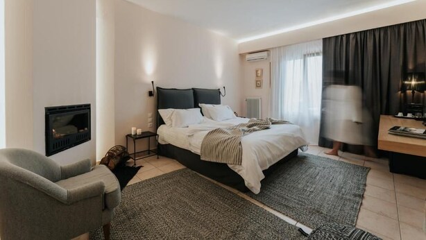 Quarto moderno com cama, mesas de cabeceira, uma poltrona, lareira e uma janela com cortinas.