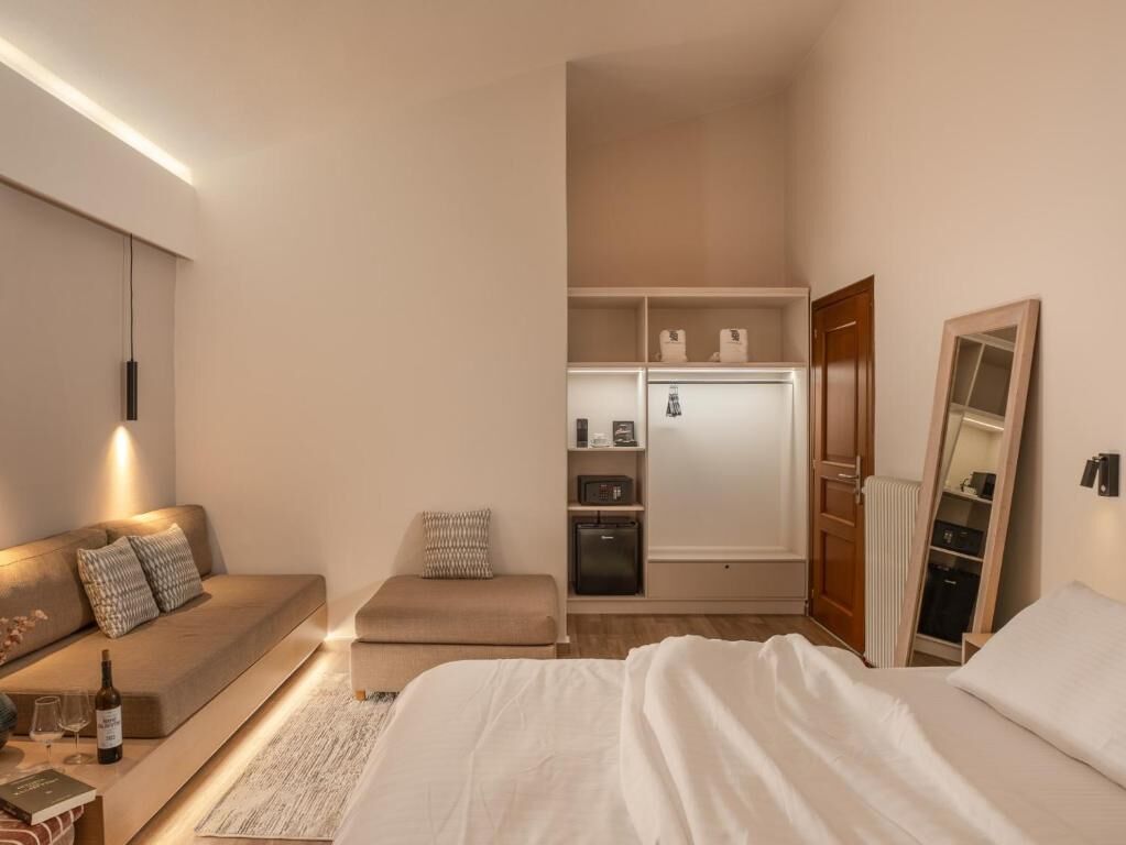 Um quarto com uma cama, um sofá, uma mesinha com uma garrafa e copos, e um guarda-roupa com espelho.