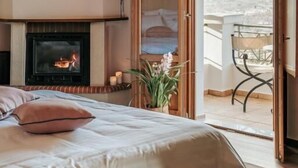 Quarto com cama, lareira, varanda com cadeira e vista para o exterior.