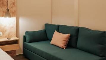 Um quarto com um sofá verde, piso de madeira e luminária pendente.