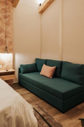 Um quarto com um sofá verde, piso de madeira e luminária pendente.