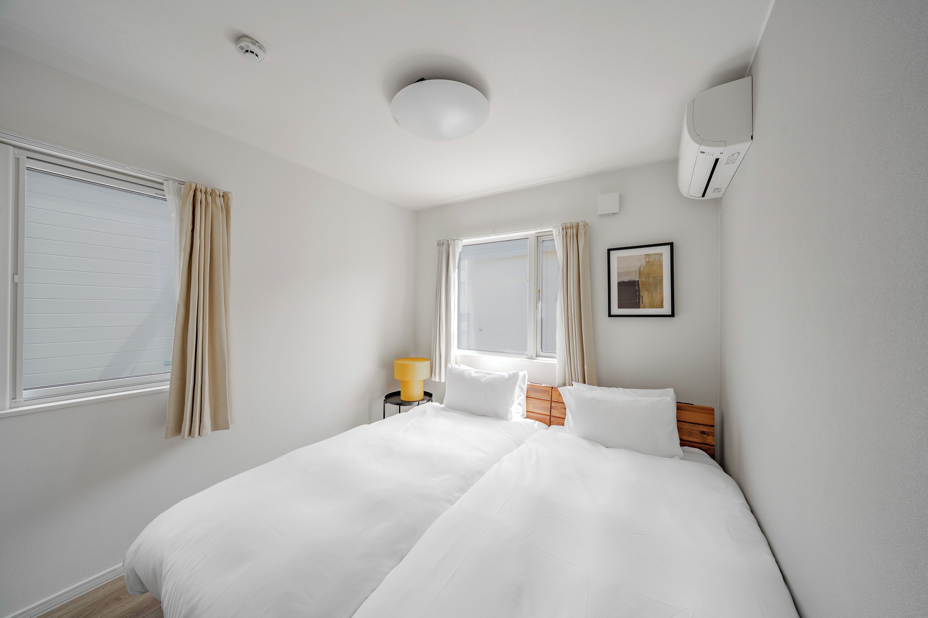 Quarto de hotel com cama, mesa de cabeceira com abajur, janela com cortinas e ar condicionado.