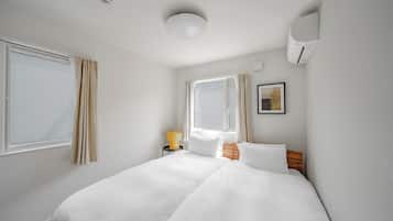 Quarto de hotel com cama, mesa de cabeceira com abajur, janela com cortinas e ar condicionado.