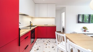Uma cozinha moderna com armários vermelhos, bancada de madeira e piso de terrazzo.