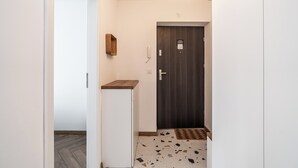 Um corredor com um banco de madeira, uma porta com código QR e um aparelho de iluminação.