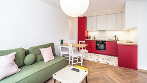 Um apartamento moderno com sofá verde, mesa de jantar branca e armários de cozinha vermelhos.