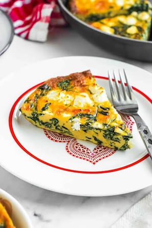 Uma fatia de quiche em um prato branco com borda vermelha.