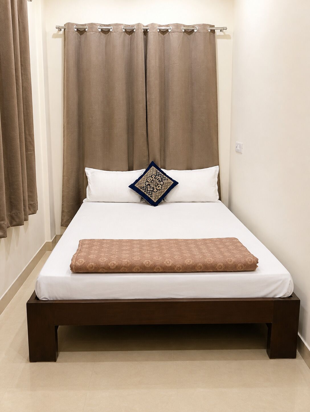 Uma cama com colchão branco, cabeceira marrom e travesseiro decorativo.