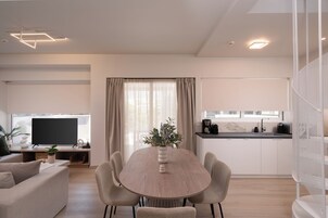 Uma sala de estar moderna com uma mesa de jantar redonda, uma TV de tela plana e uma área de cozinha com cafeteira.