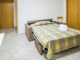 Uma cama de solteiro com um edredom, um banco de madeira e uma porta.