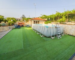 Uma piscina ao ar livre com muro de pedra, rodeada por grama sintética e equipada com várias espreguiçadeiras.